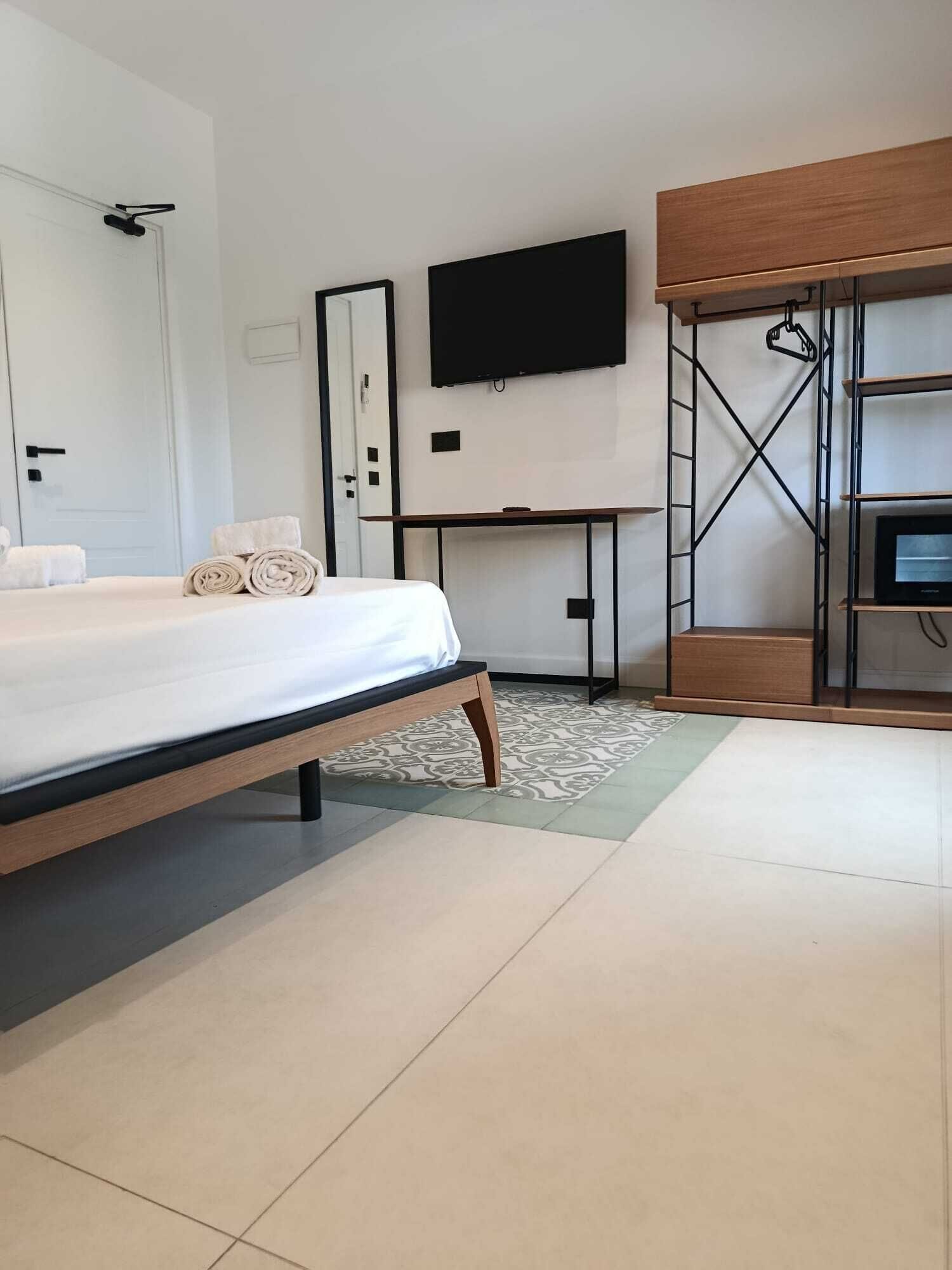 Quarto de hotel com uma cama, uma escrivaninha, uma televisão e um guarda-roupa.