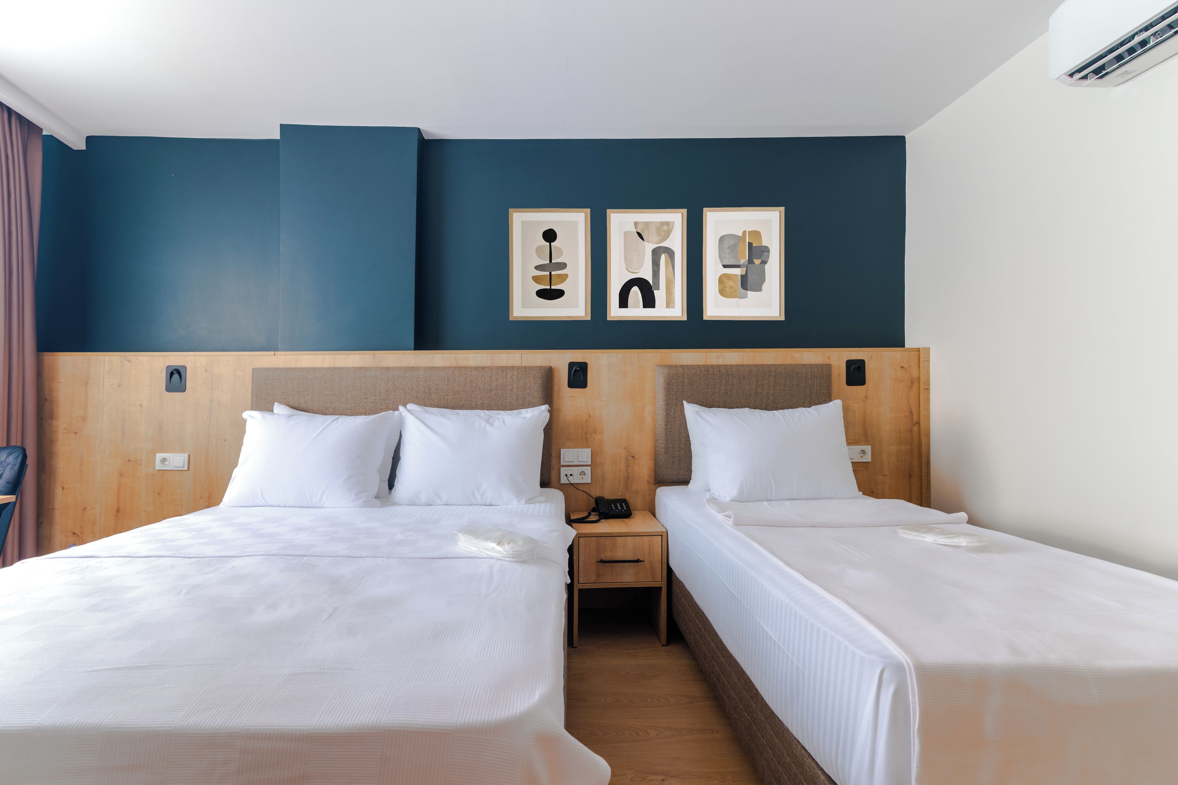 Quarto de hotel com duas camas, cabeceira de madeira, mesa de cabeceira com telefone e uma obra de arte na parede.