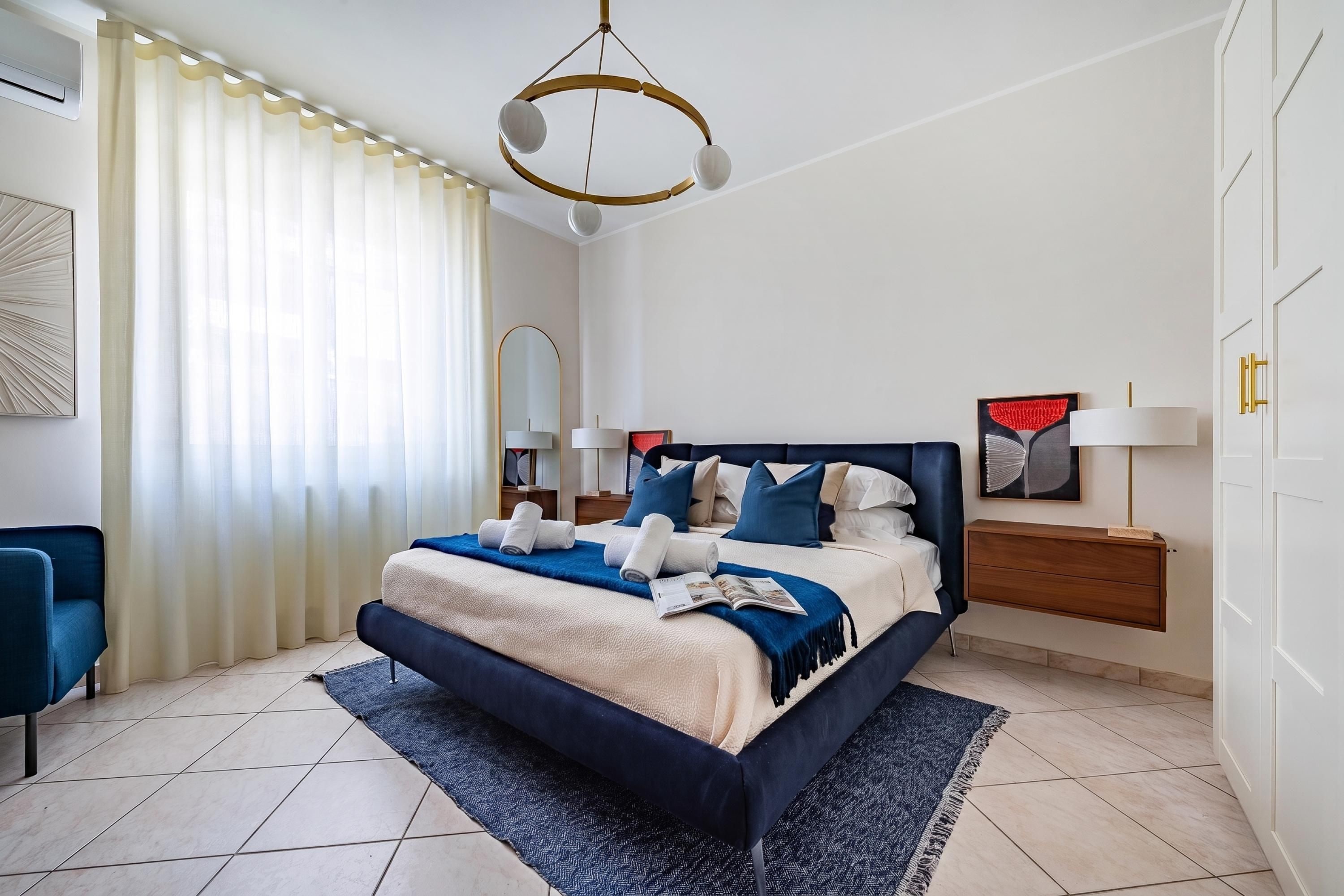 Quarto moderno com cama grande, mesa de cabeceira, luminária de teto e uma cadeira.