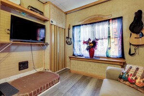 Uma sala de estar com televisão, uma janela e um banco, além de um violão.