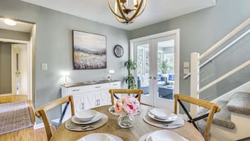 Uma sala de jantar com uma mesa de madeira posta para quatro pessoas, um lustre e um quadro na parede.