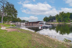 Um edifício à beira do lago com um cais, cercado por árvores e uma área gramada.