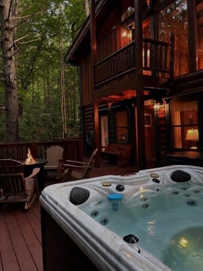 Uma cabana de madeira com hidromassagem em um deck rodeado por árvores.