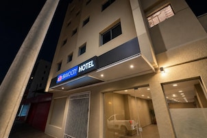 Entrada de hotel com uma placa que diz 'BRAVOARY HOTEL' e uma porta de vidro que dá acesso ao interior.