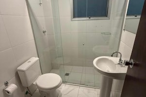 Casa de banho com chuveiro em cabine de vidro, sanita e lavatório.