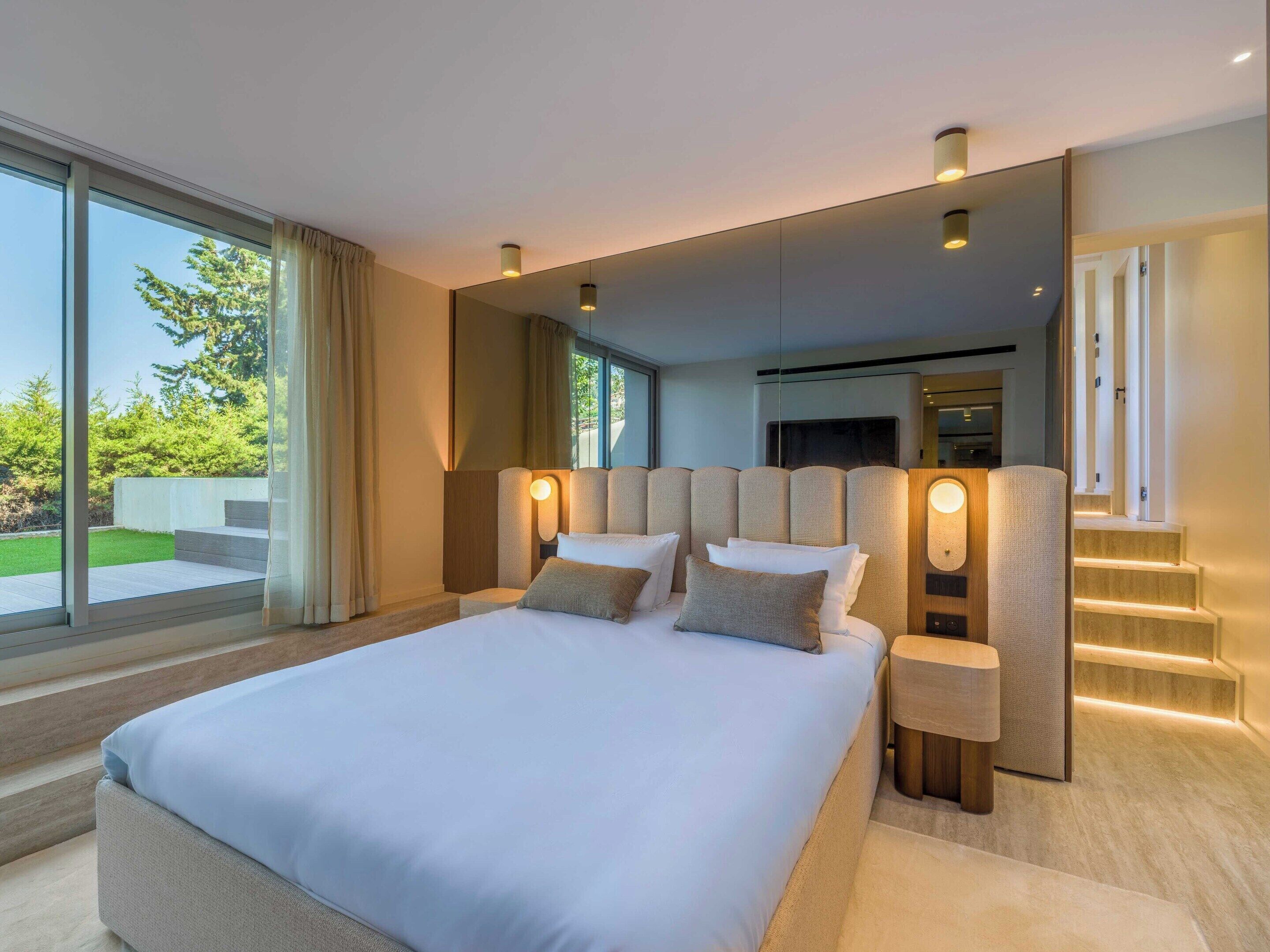 Quarto de hotel moderno com uma cama grande, televisão e vista para o exterior.