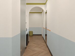 Um corredor com piso em padrão herringbone, paredes brancas com uma faixa azul clara e uma parede de destaque verde.