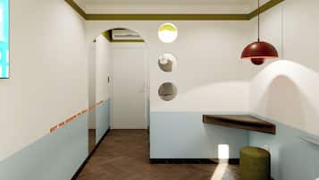 Quarto de hotel com uma cama, um espaço de estar pequeno, uma estante na parede e um corredor que dá para outro quarto.