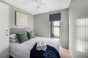 Quarto com cama, almofadas, cobertor, ventilador de teto e janela com persianas.