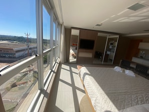 Quarto de hotel com uma janela grande, uma cama, uma televisão e uma kitchenette.