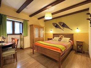 Quarto com cama de madeira, escrivaninha com cadeira, janela com cortinas e luminárias na parede.