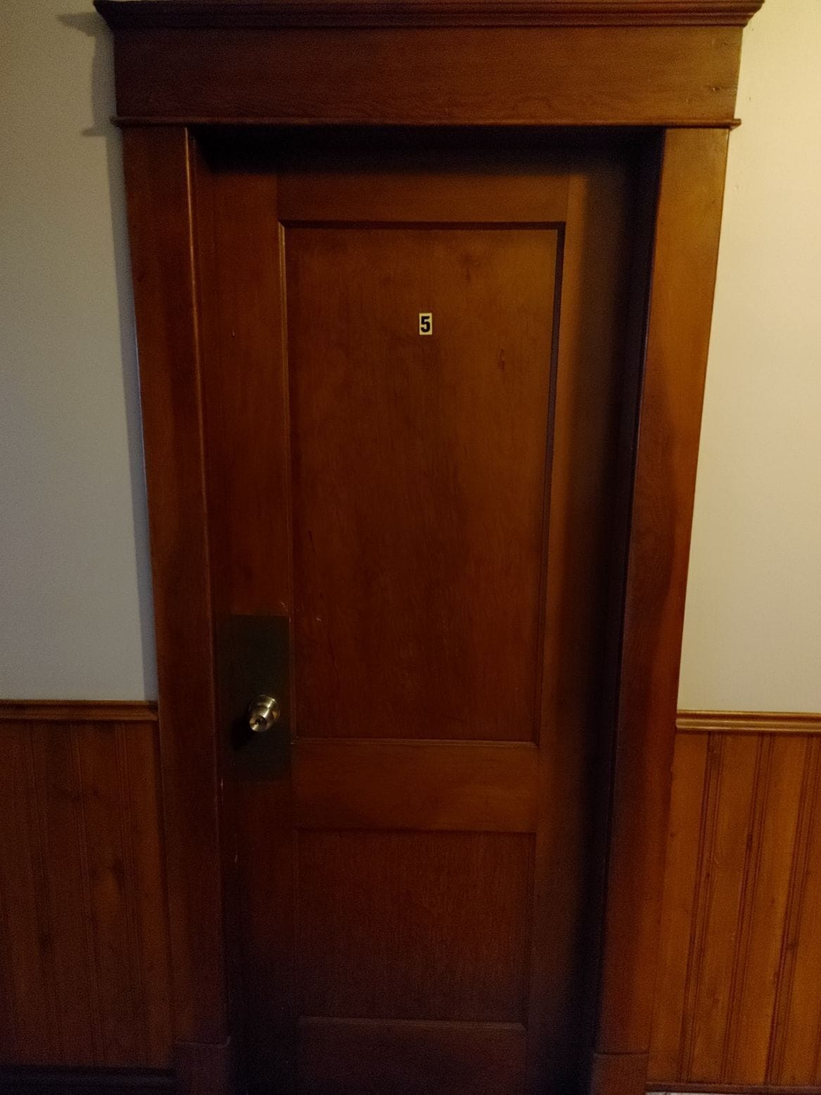 Uma porta de madeira com maçaneta de latão e um pequeno adesivo com o número 5.