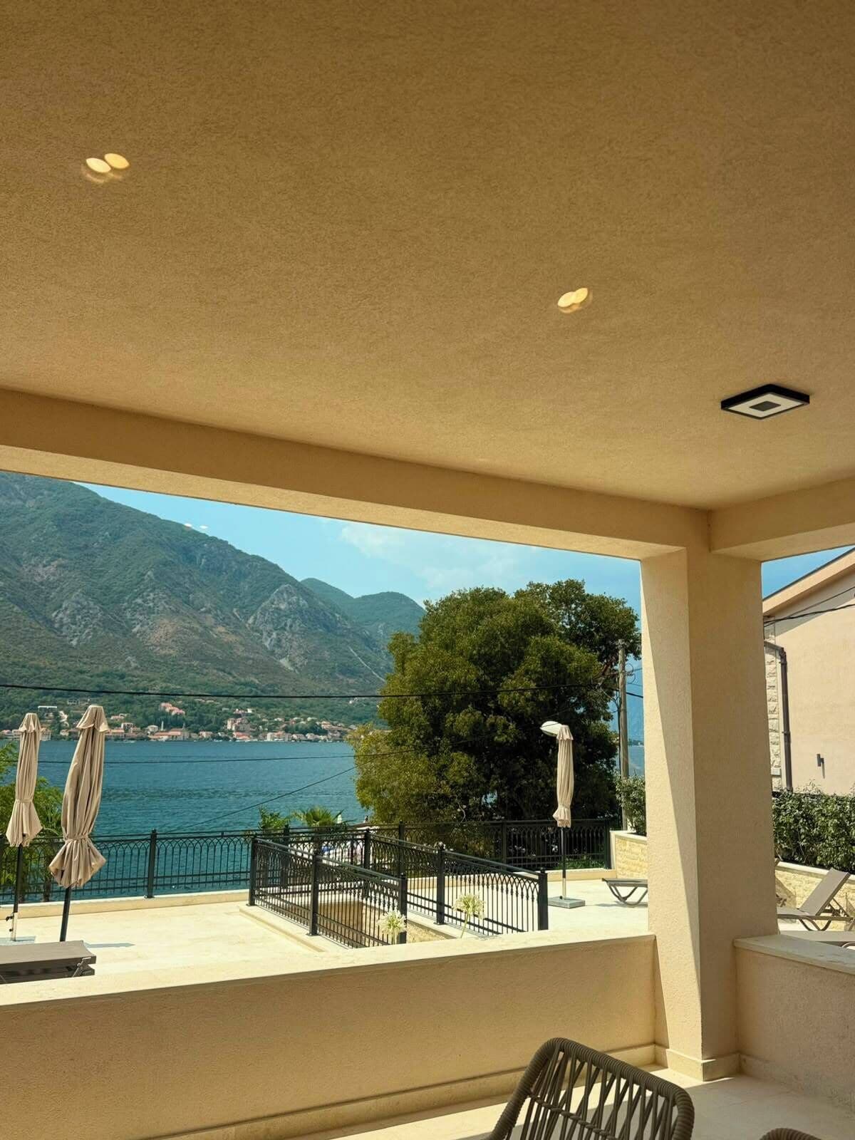 Varanda com vista para um lago e montanhas, mobiliário de exterior e guarda-corpo.