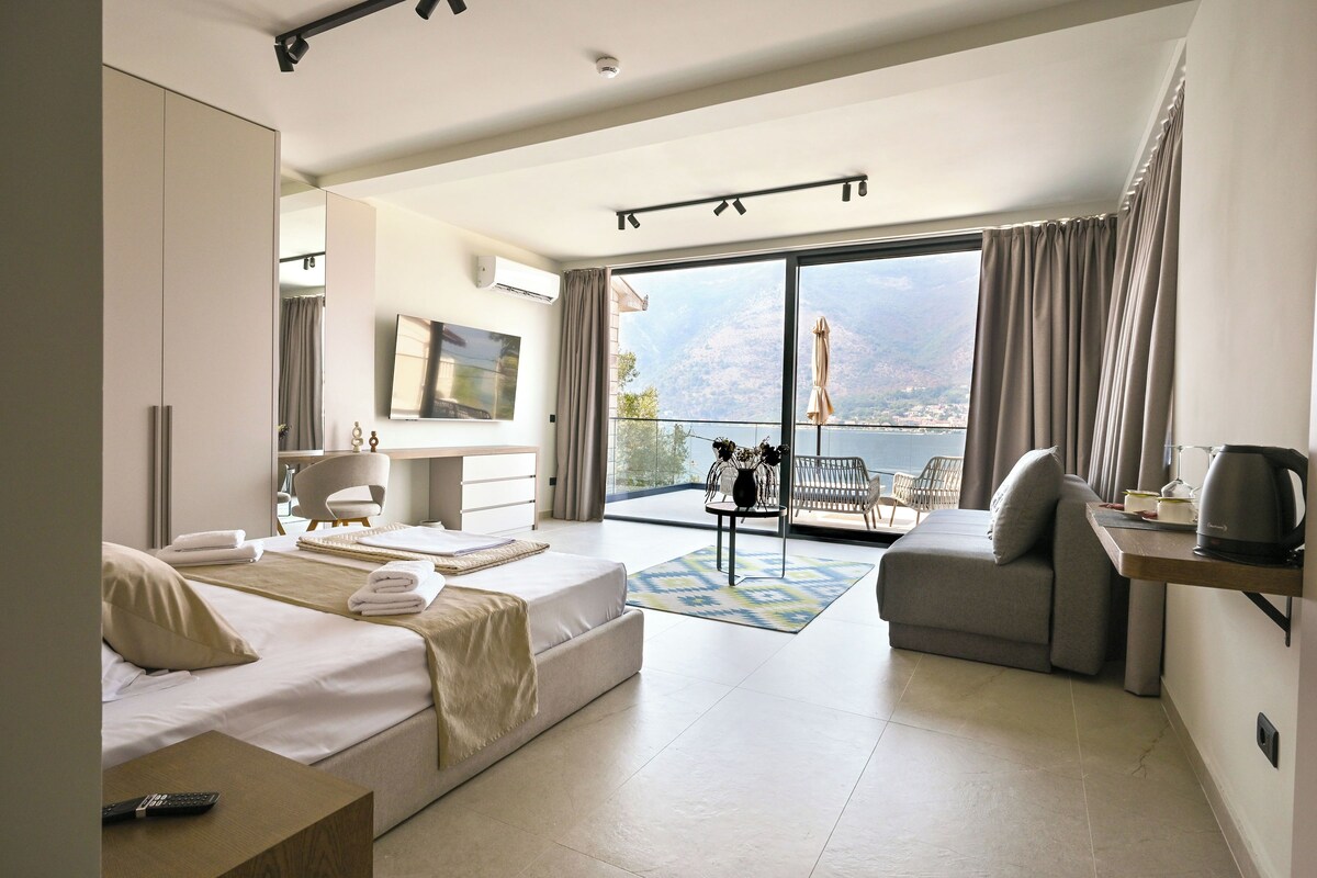 Quarto de hotel moderno com varanda, sofá, escrivaninha e televisão.