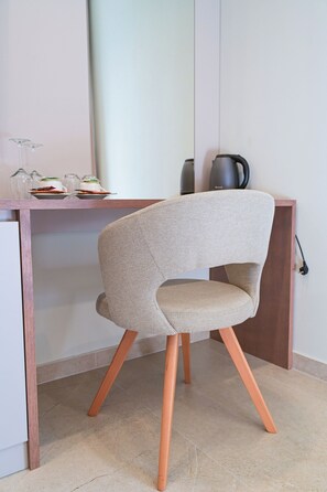 Uma cadeira moderna com encosto trançado e pés de madeira, colocada em frente a uma escrivaninha com um laptop e uma chaleira.
