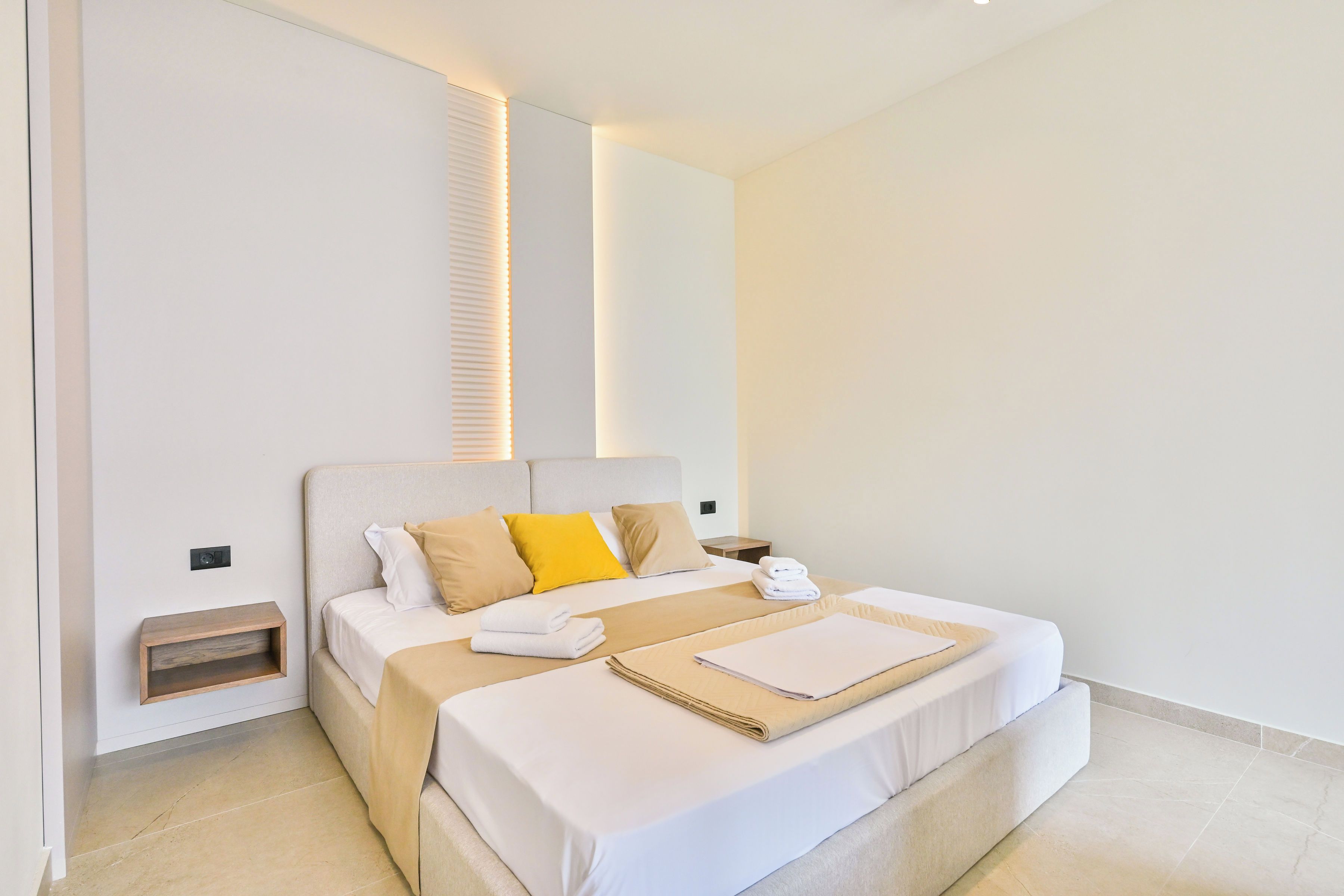 Quarto de hotel moderno com uma cama grande, uma mesinha de cabeceira e um criado-mudo.