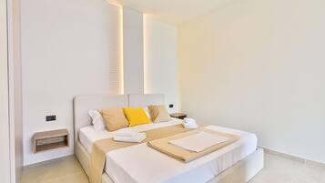 Quarto de hotel moderno com uma cama grande, uma mesinha de cabeceira e um criado-mudo.