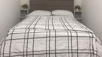 Uma cama com cabeceira, um edredom quadriculado preto e branco e duas mesas de cabeceira com plantas.