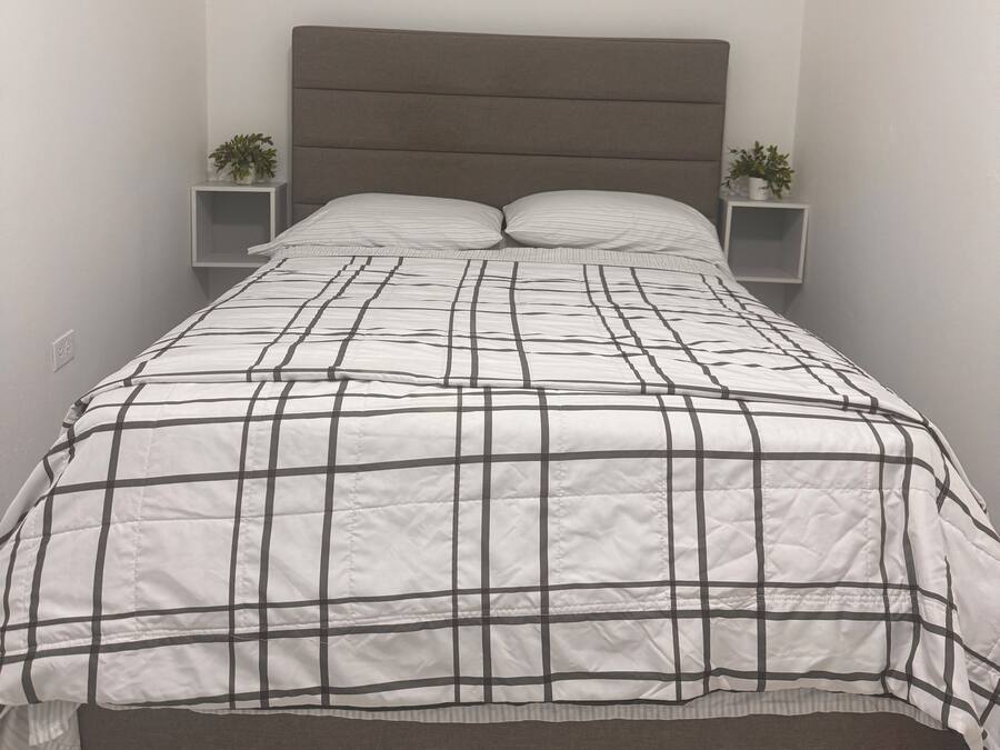 Uma cama com cabeceira, um edredom quadriculado preto e branco e duas mesas de cabeceira com plantas.
