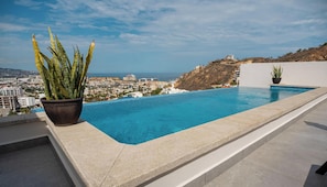 Piscina infinita no terraço com vista para um horizonte costeiro e uma colina com edifícios.