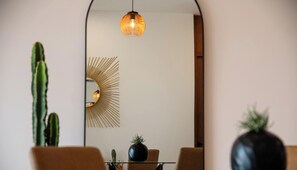 Um interior moderno com uma área de jantar, uma planta de cacto, um espelho redondo e um lustre.
