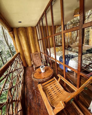 Um deck de madeira com mesa e cadeiras, um vaso de planta e uma janela com vista para árvores.