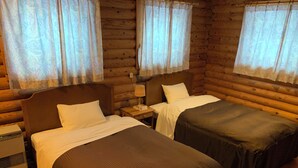 Quarto de cabana rústica com duas camas, paredes de madeira e janela com cortinas.
