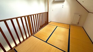 Quarto com esteiras de tatame, guarda-corpo de madeira, radiador e ar condicionado fixado na parede.