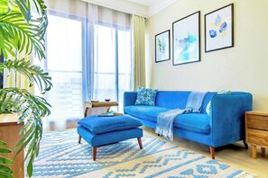 Uma sala de estar com um sofá azul, um banquinho combinando e um tapete estampado.