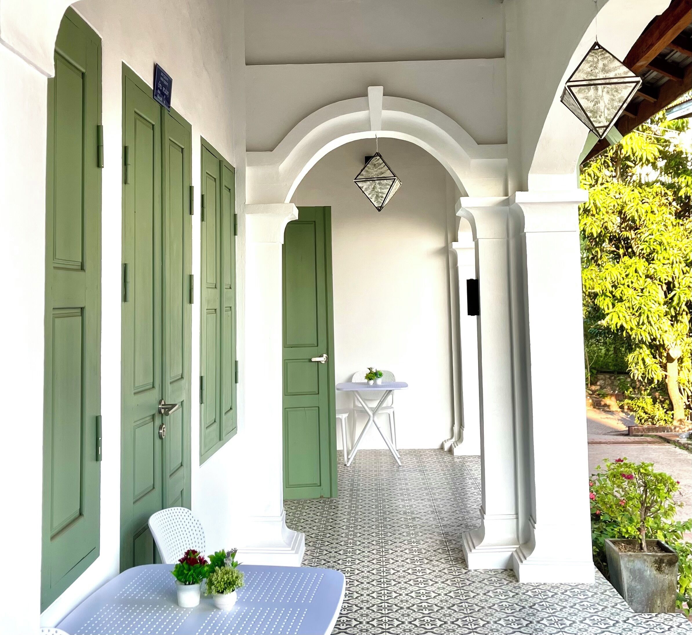 Uma área externa coberta com uma mesa, cadeiras, um vaso de planta e piso de azulejos.