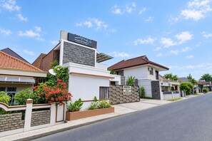 Rua residencial com casas modernas, céu claro e uma placa com a inscrição 'House Of Tuwuh'.