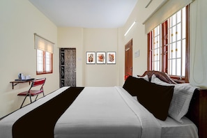 Quarto de hotel com uma cama, uma escrivaninha com cadeira e uma janela com cortinas.