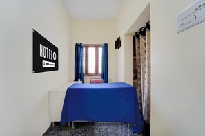 Quarto de hotel pequeno e individual, com cama, janela com cortinas, TV fixada na parede e placa indicando serviço OYO.