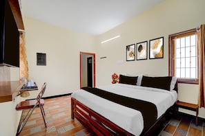 Quarto de hotel com cama, escrivaninha, cadeira, janela com cortinas e porta.