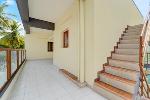 Um edifício residencial com uma escadaria que leva a um andar superior, uma varanda com guarda-corpo e piso revestido de azulejos.
