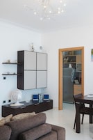 Uma sala de estar moderna com um sofá marrom escuro, uma mesa de consola branca e uma área de refeições com mesa e cadeiras de madeira.