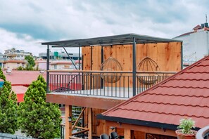 Um edifício de madeira com varanda, escadaria e cadeira suspensa.