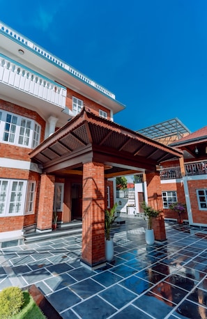 Um pátio amplo com entrada coberta, um edifício de tijolos com grandes janelas e um céu azul claro.