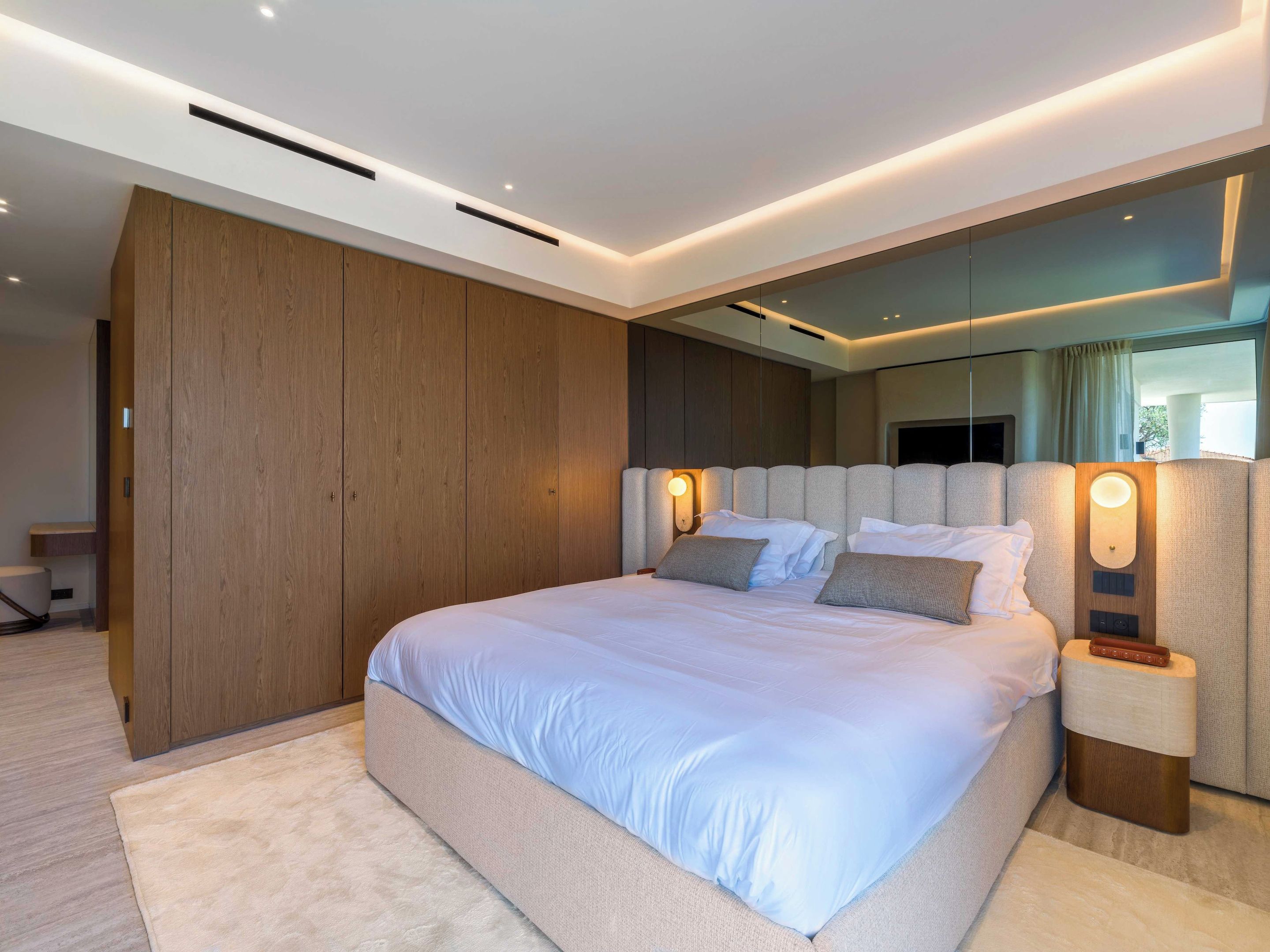 Quarto moderno com uma cama grande, guarda-roupa de madeira e um espelho.