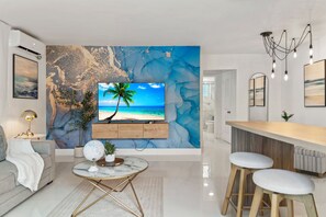Uma sala de estar moderna com uma TV grande presa em uma parede texturizada, um sofá, uma mesa de centro e um espaço de bar com banquetas.