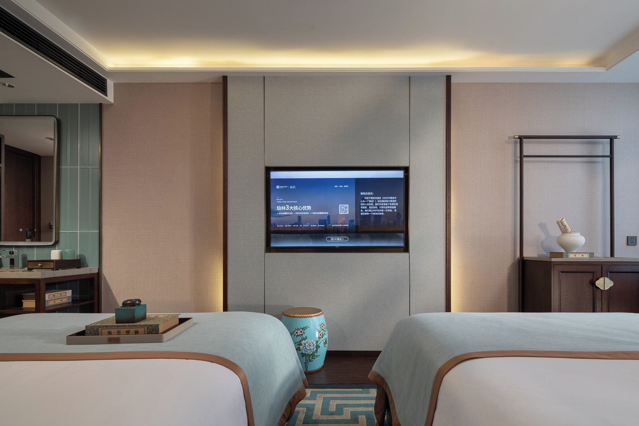 Quarto de hotel com duas camas, televisão presa à parede, mesa lateral pequena e armário com um vaso.