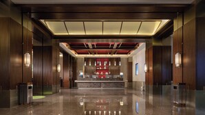 Um lobby moderno com balcão de recepção, painéis de madeira e piso de mármore polido.