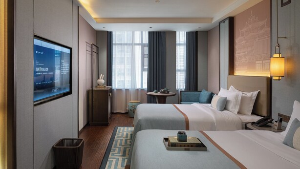 Quarto de hotel com duas camas, televisão, uma pequena mesa com chaleira e uma luminária decorativa.