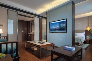 Quarto de hotel com cama, secretária, televisão e área de estar.