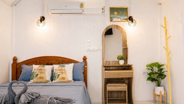 Quarto com cama, cômoda, espelho, ar condicionado fixado na parede e planta em vaso.