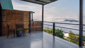Varanda com vista para nuvens e vegetação, parede de bambu e mesa com cadeiras.
