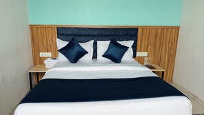 Quarto de hotel com cama, duas mesas de cabeceira, cabeceira de madeira e parede lisa.