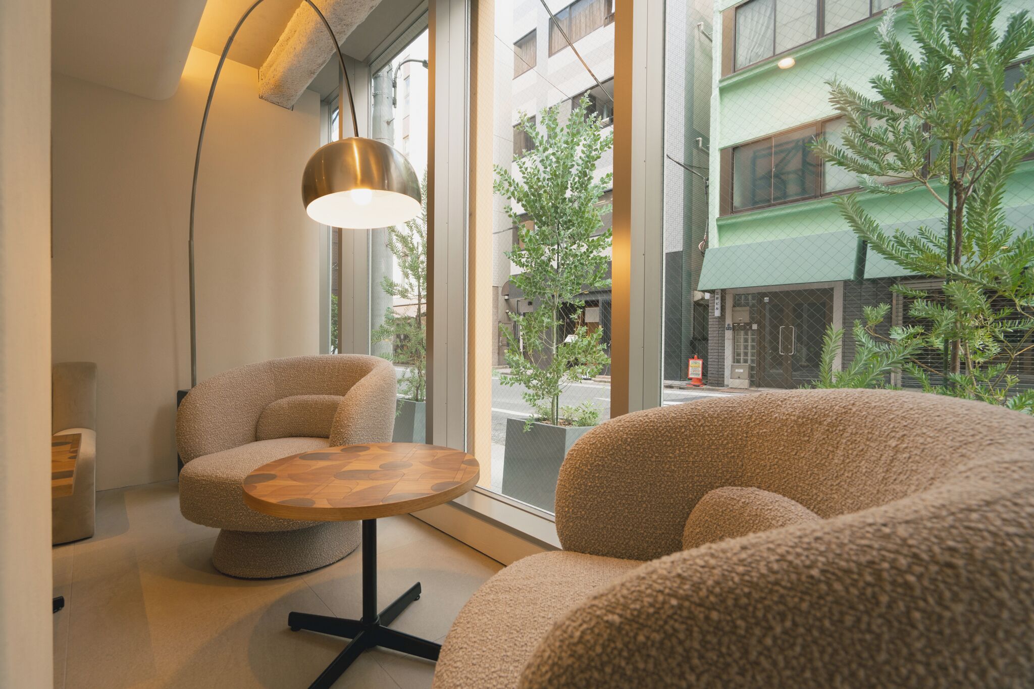 Um interior moderno com uma mesa de madeira redonda, duas poltronas bege e uma luminária pendente.