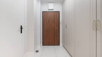 Um corredor com paredes brancas, uma porta de madeira no final e chão de azulejos brancos.