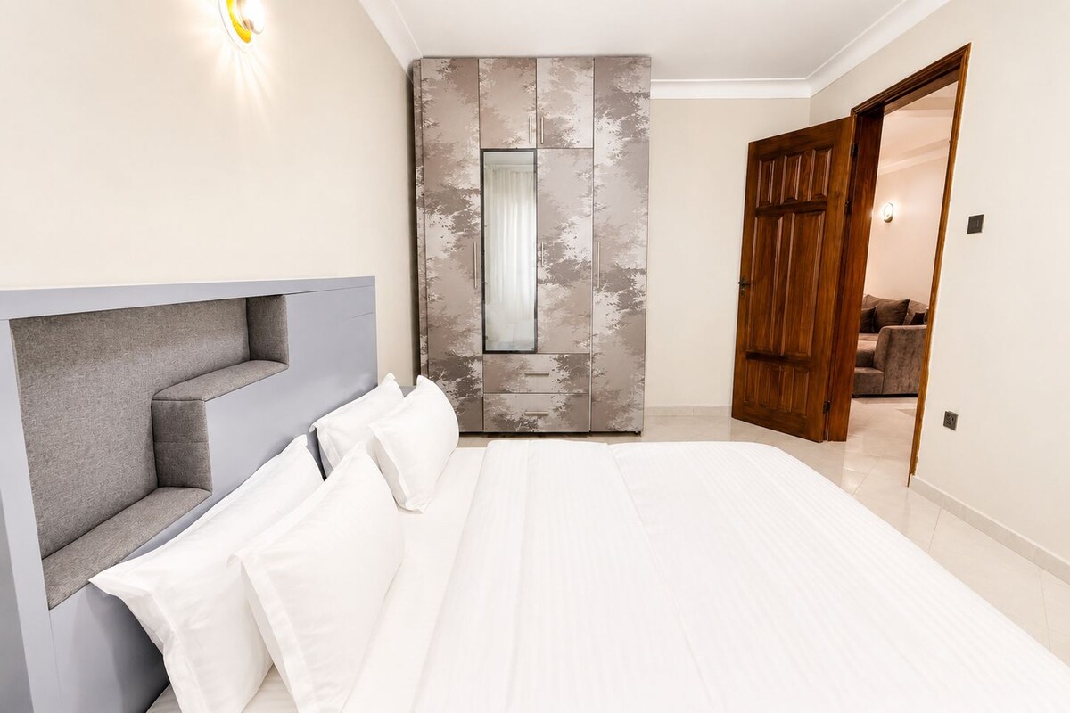 Quarto moderno com uma cama grande, um banco embutido, guarda-roupa e espelho.